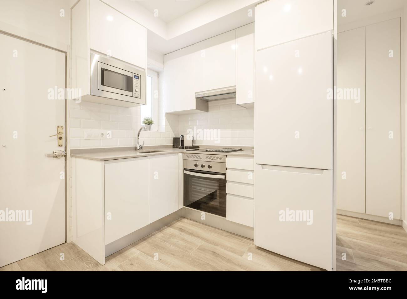 Small open plan corner kitchen with white handleless cabinets and a ...