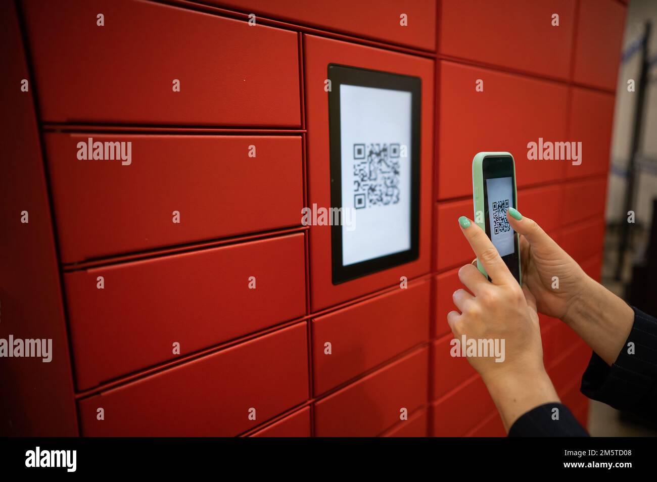 A woman scans a red code to pick up a parcel at a parcel machine ...