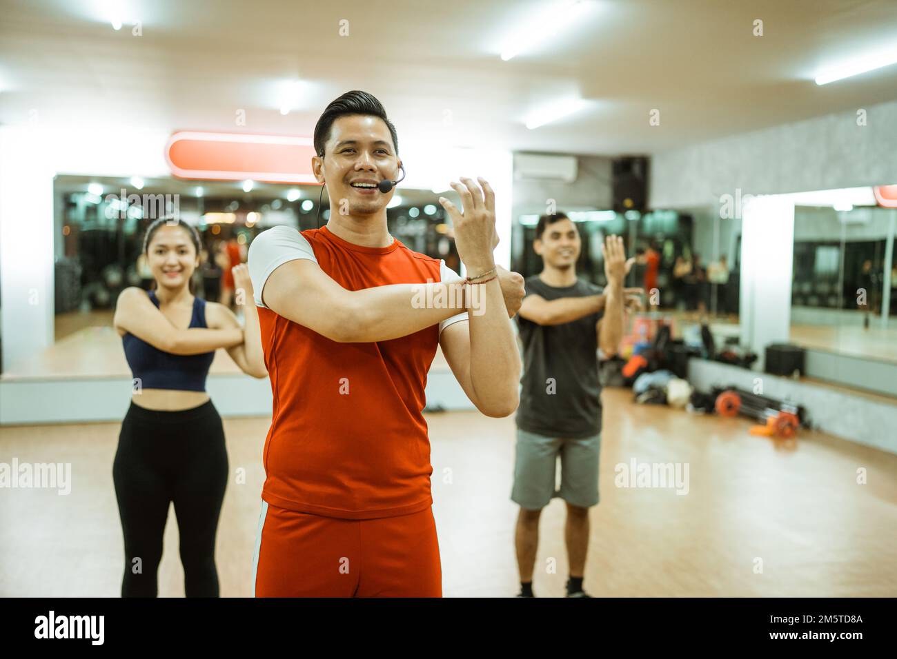 male instructor leading a group with arm muscle stretching movements ...