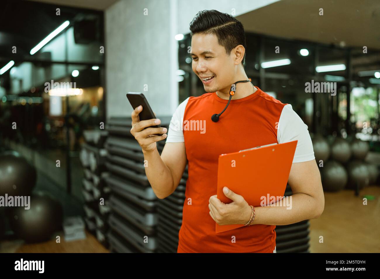 male instructor standing holding clipboard while using mobile phone ...