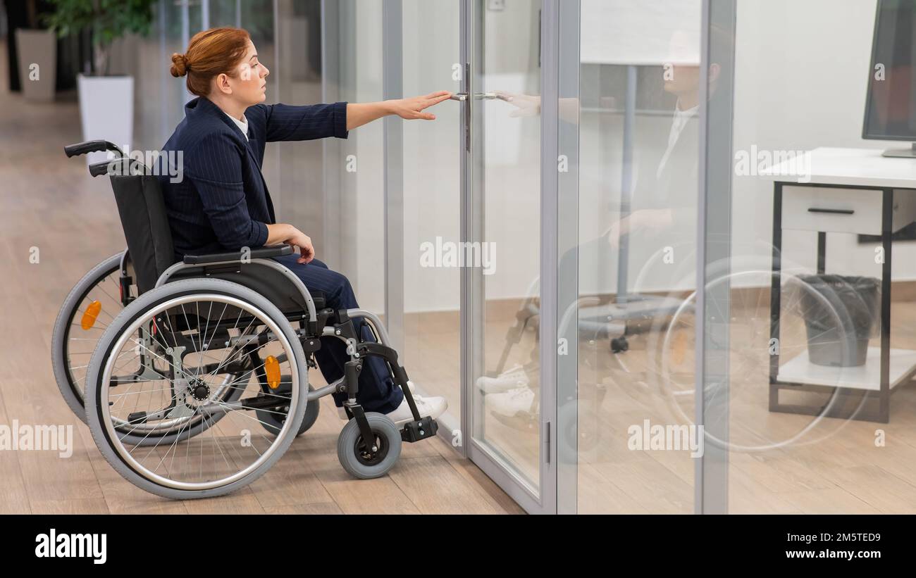 Red-haired caucasian woman in a wheelchair trying to open the door in ...