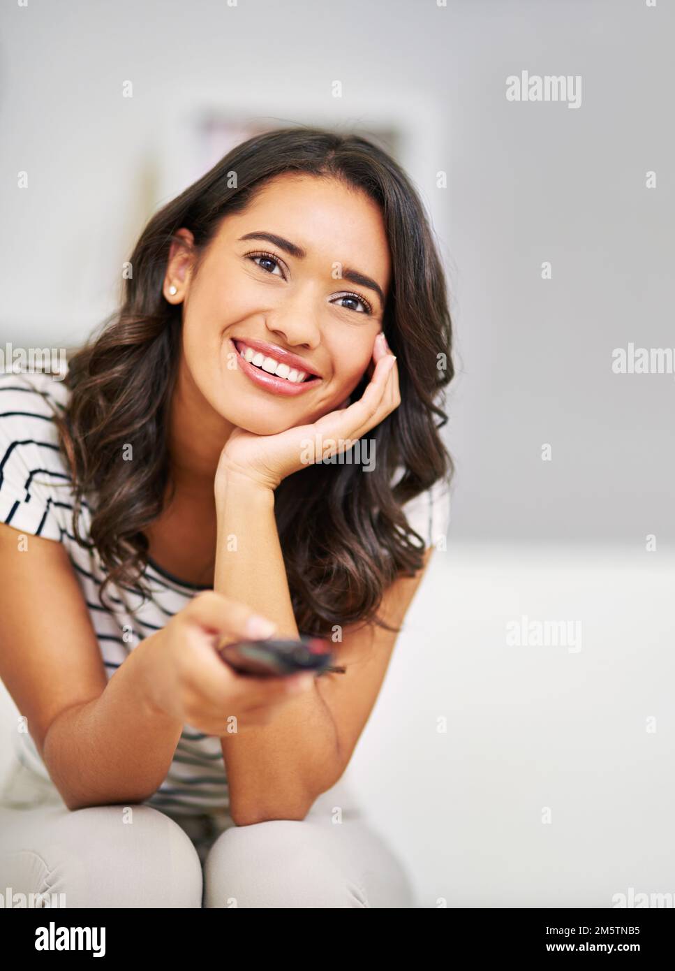 Whats on TV. a young woman watching TV while relaxing on her sofa at ...