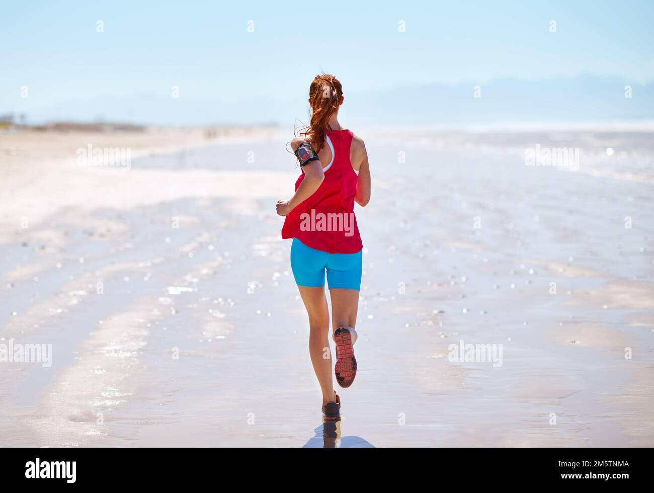 Getting her fitness on at the beach. Rearview shot of a young woman ...