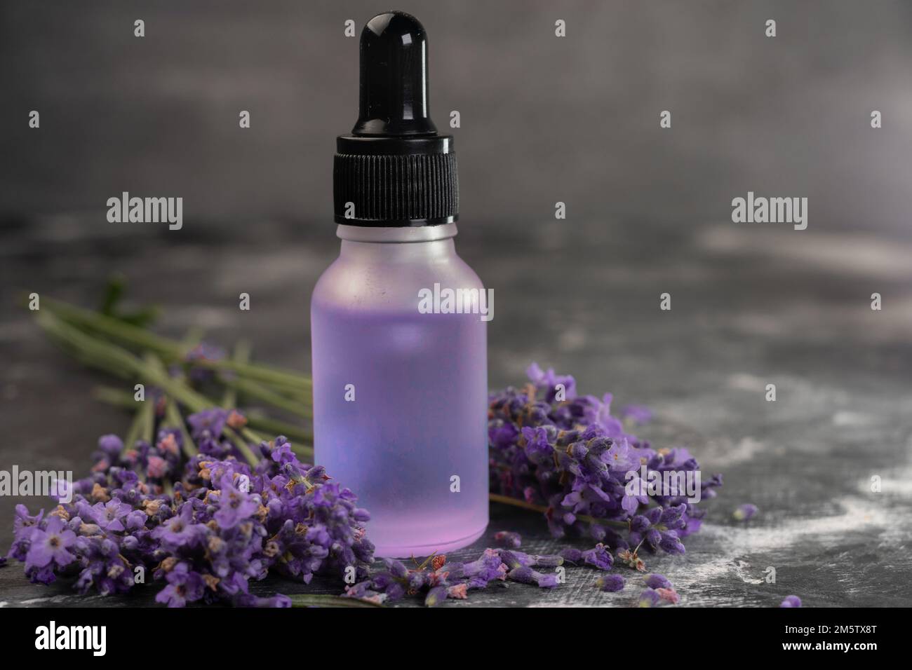 Dropper bottle of essential lavender oil, mortar of dry lavender flowers on table. Bottle with ...