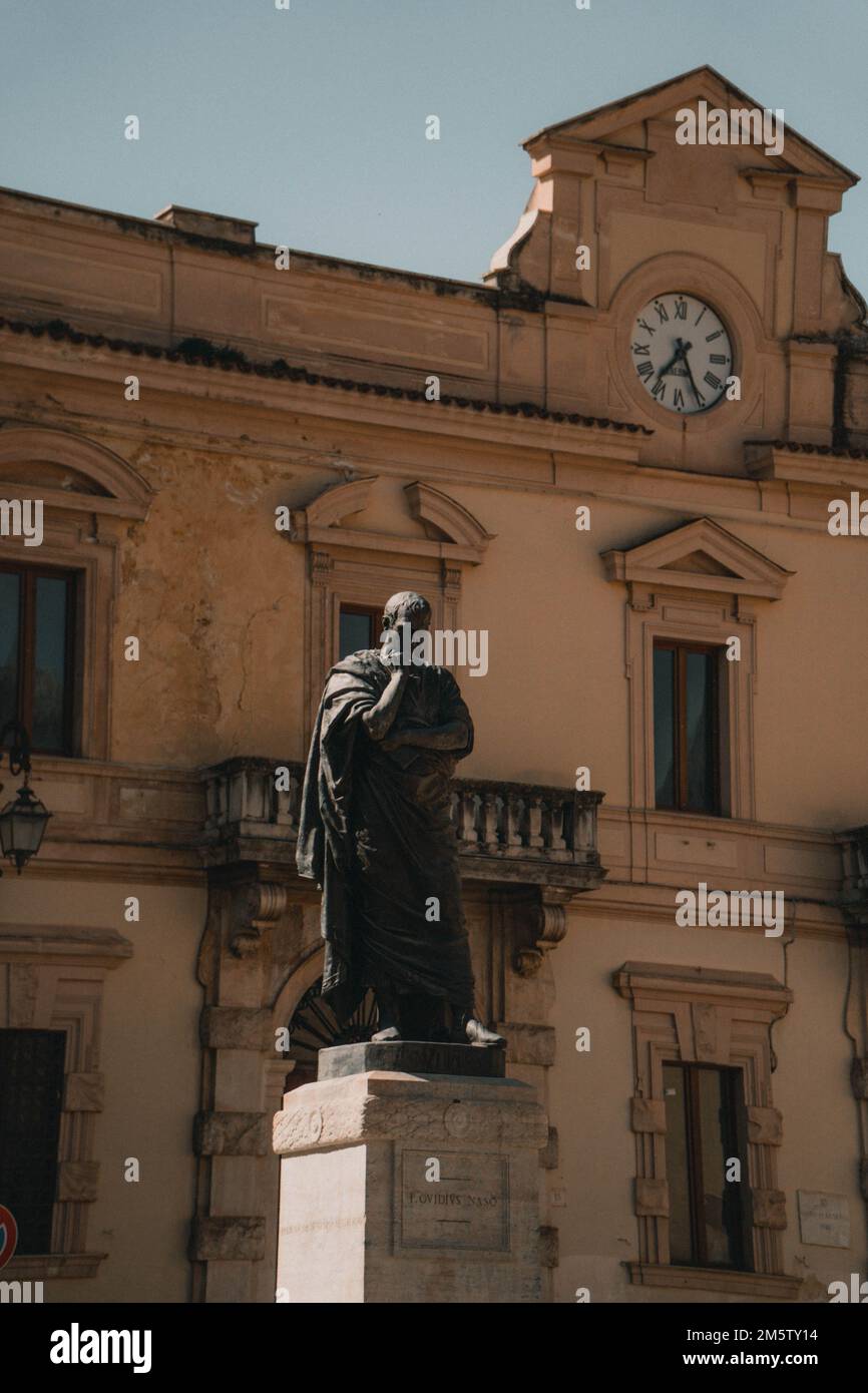 A vertical of Ovid's Statue in a beautiful square with a clock building ...