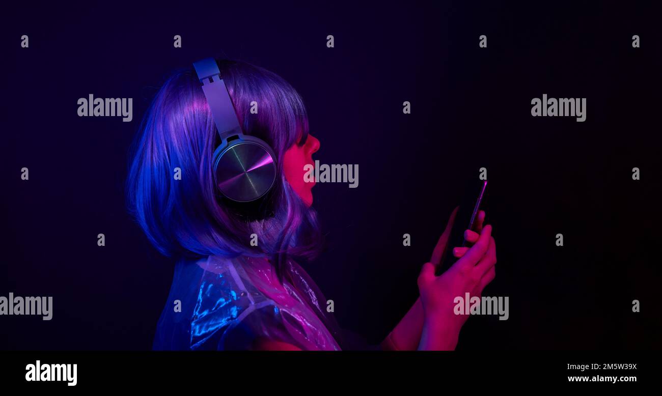 Woman in headphones listening music and enjoing in purple neon lights ...
