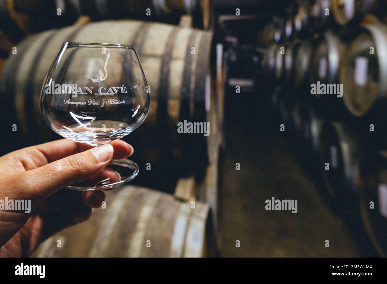 Glass with Jean Cavé's Armagnac inscription in a cellar full of barrels ...