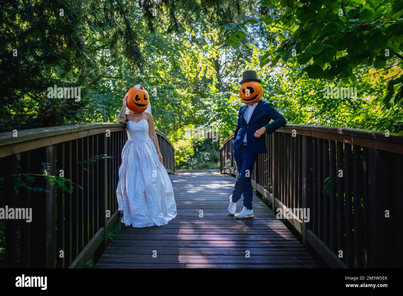 A bride and groom wearing scary pumpkin heads and standing on a bridge ...