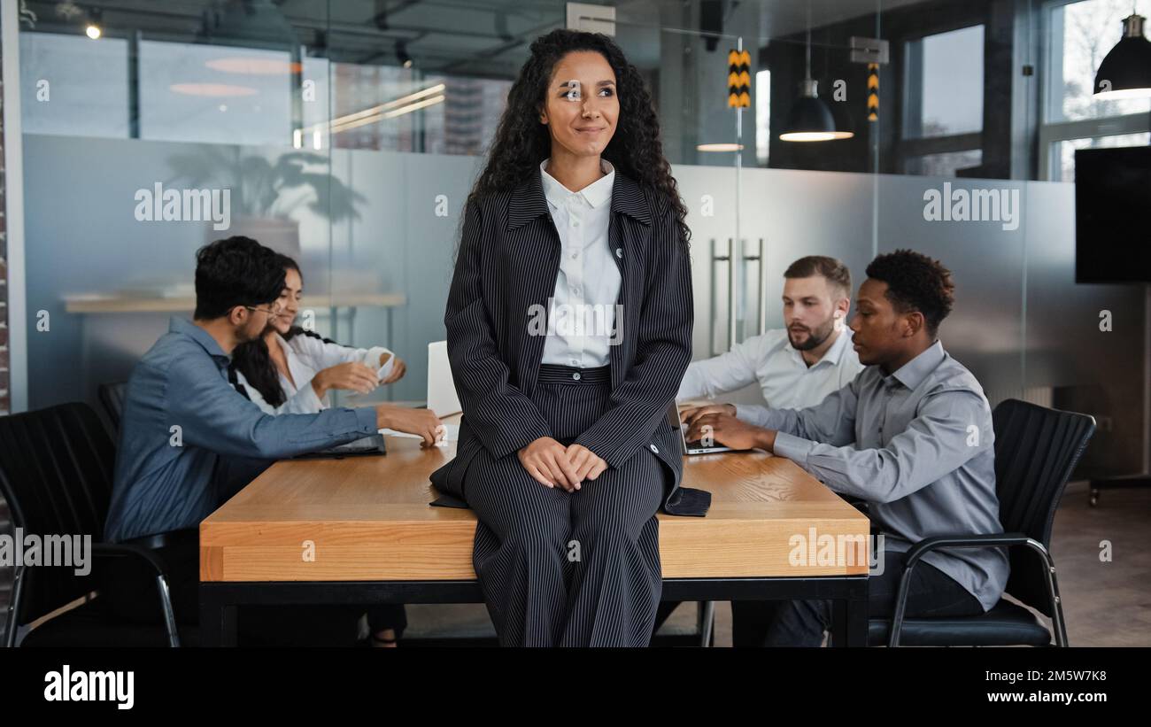 Pensive smiling businesswoman female leader boss woman sitting on table ...
