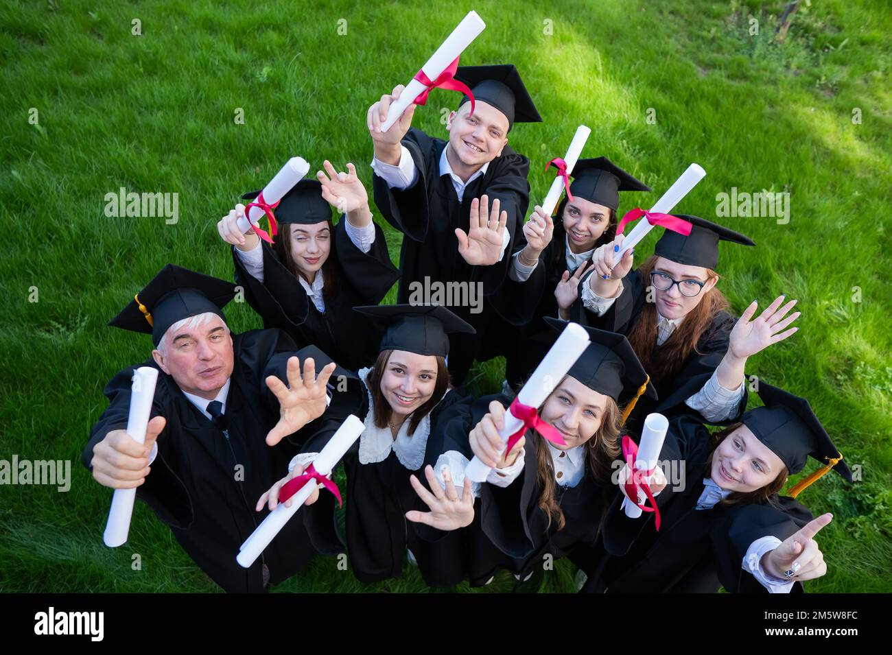 Graduates in robes show off their diplomas outdoors. View from above ...