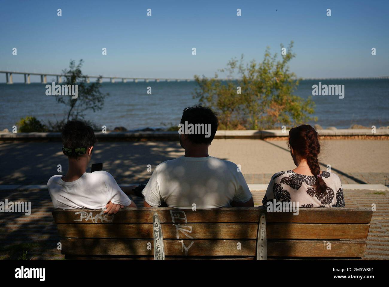 Three people looking over the sea from a bench Stock Photo - Alamy