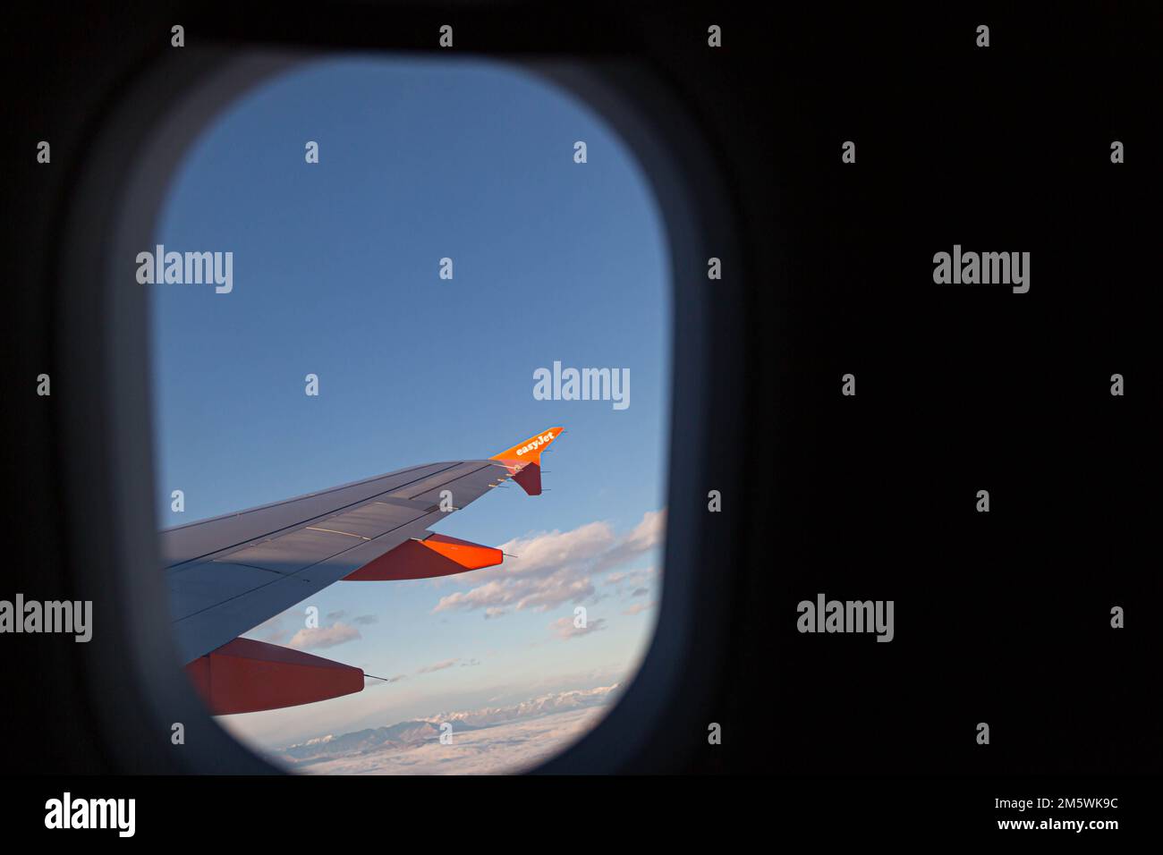EasyJet airplane wing visible from cabin window over clouds. Air travel ...