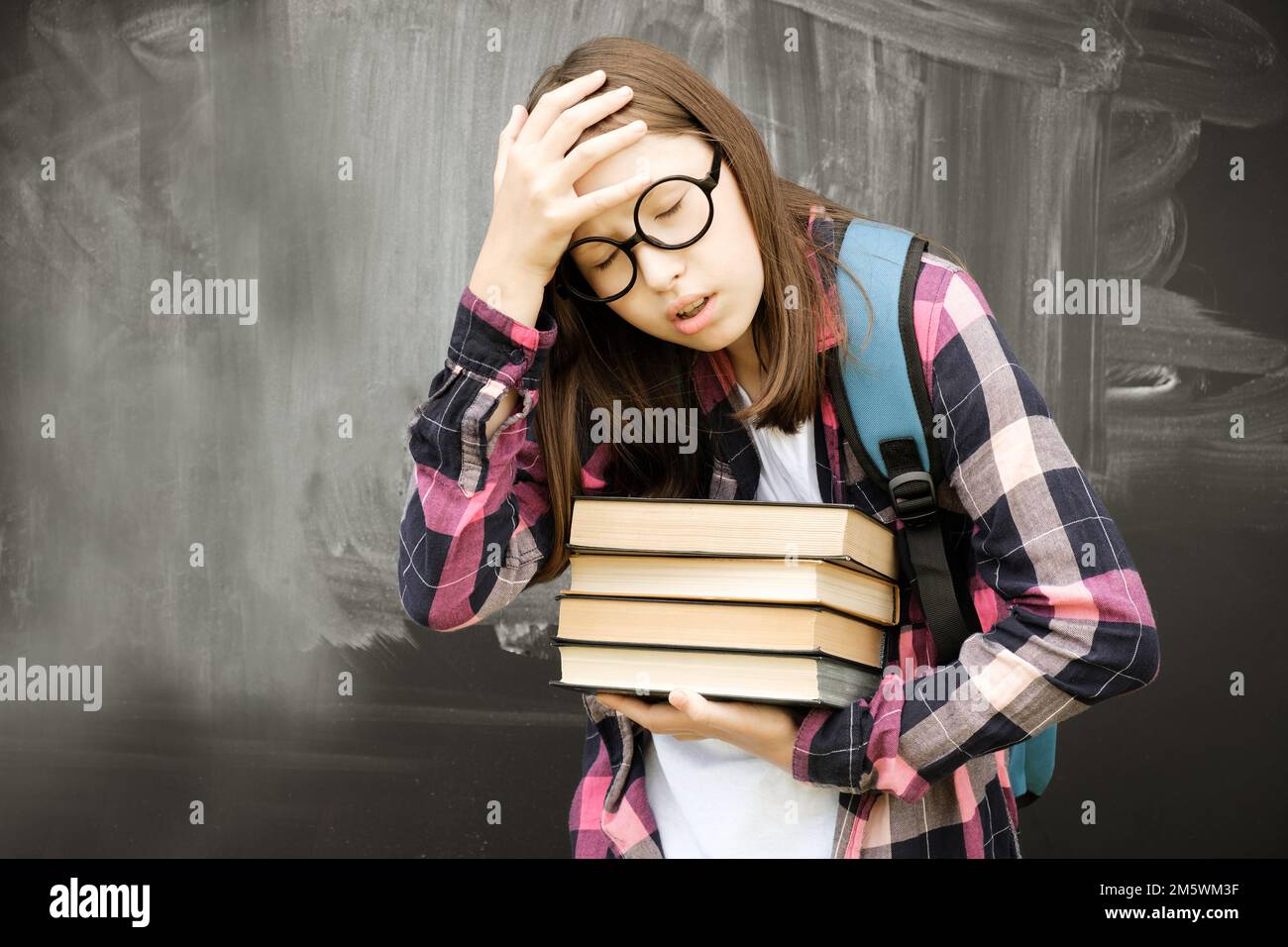 Teen girl little student holding pile of heavy books on chalkboard ...