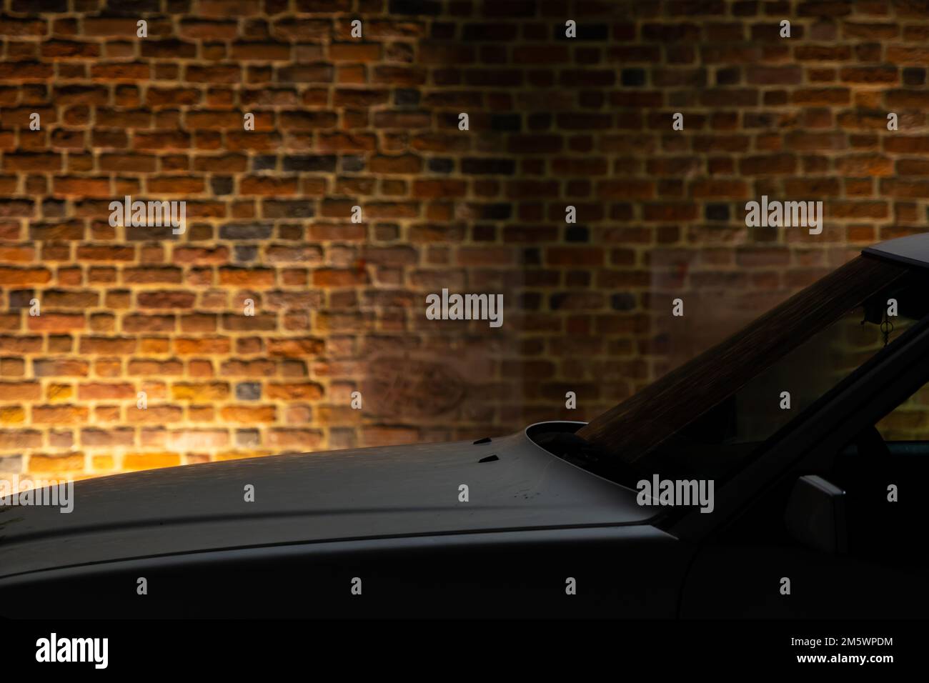 A white car parked at night against an illuminated red brick wall. View ...