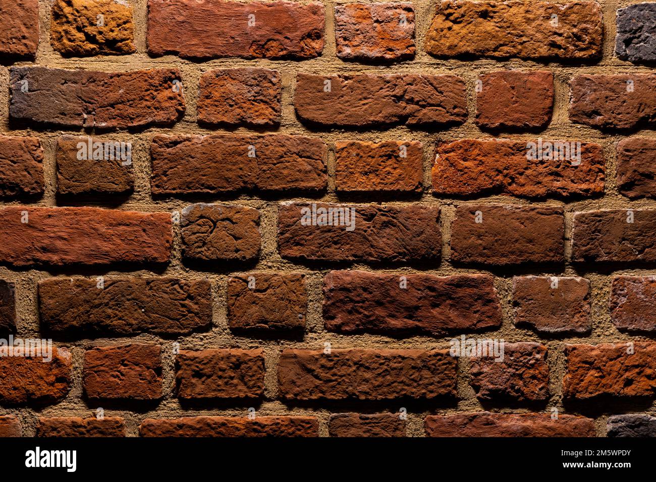 A red brick wall illuminated at night. Surface texture emphasized by ...