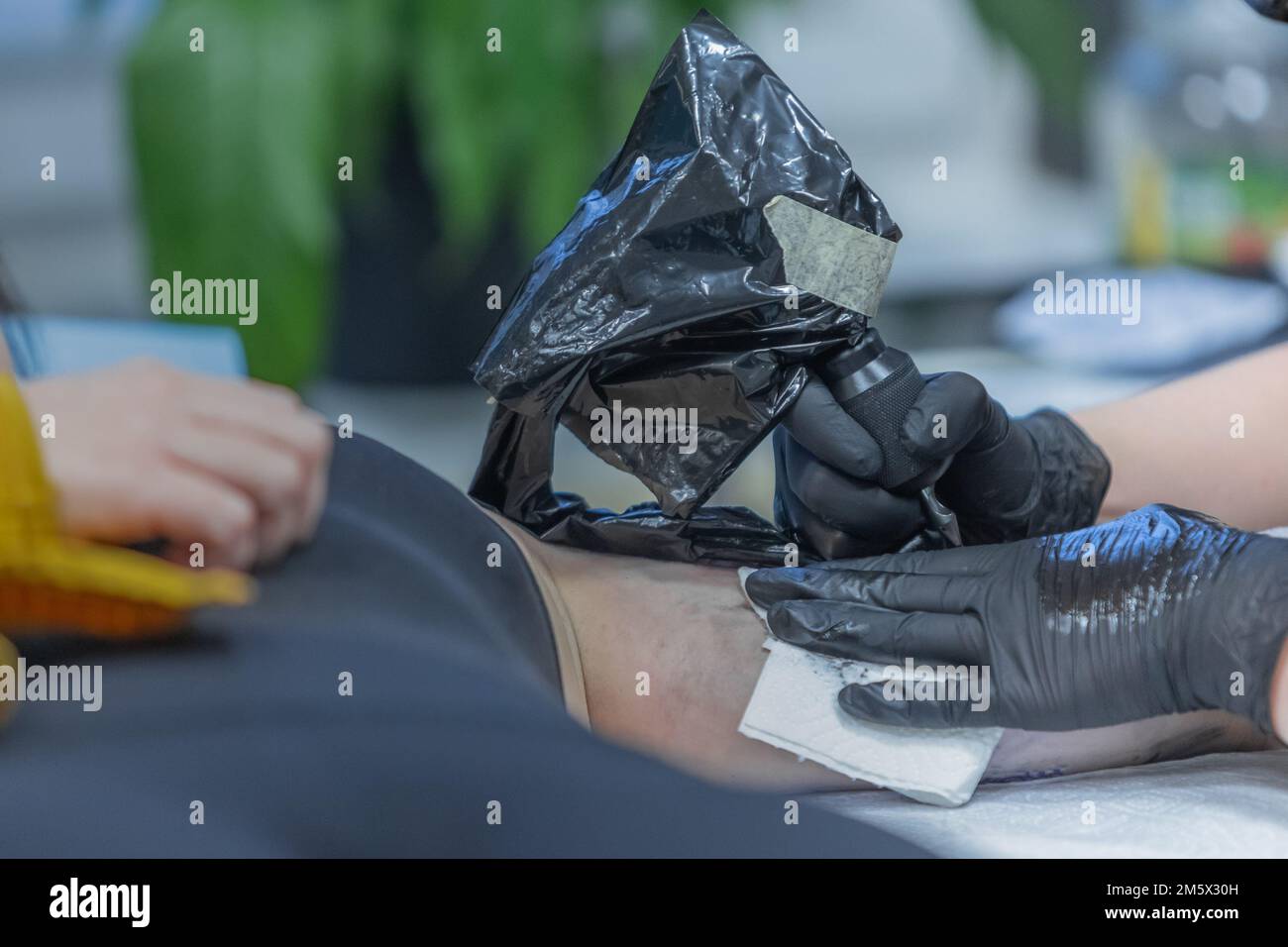 Tattoo artist at work. Visible hands in black gloves holding tattoo gun ...