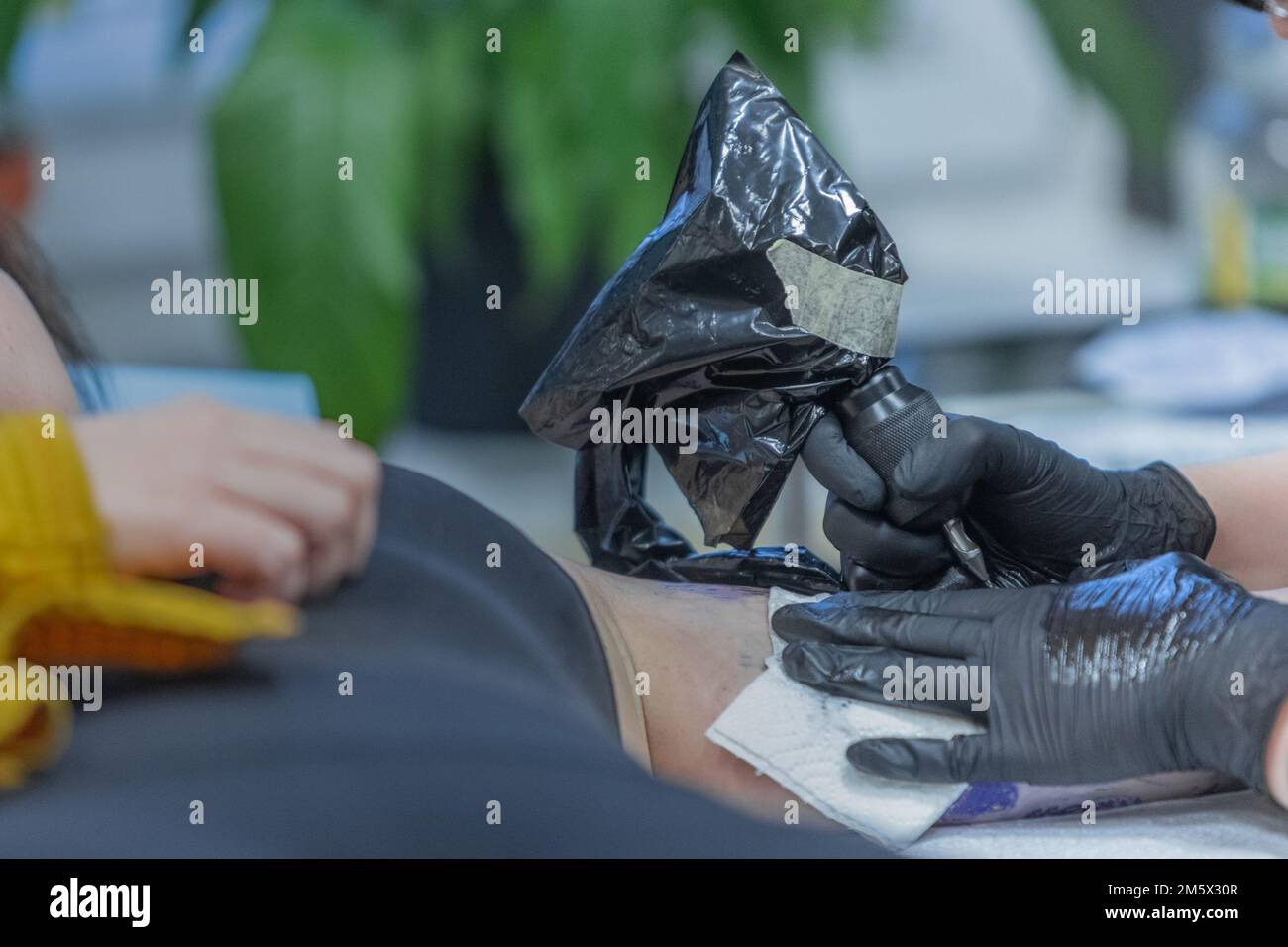 Tattoo artist at work. Visible hands in black gloves holding tattoo gun ...