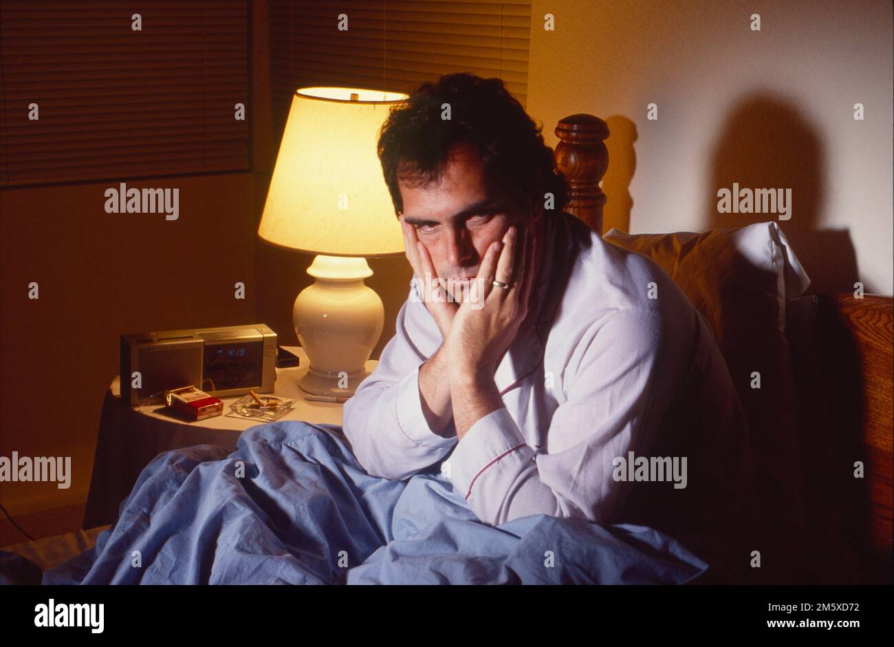 Man depressed lying in bed hands to his face, looking dejected and ...