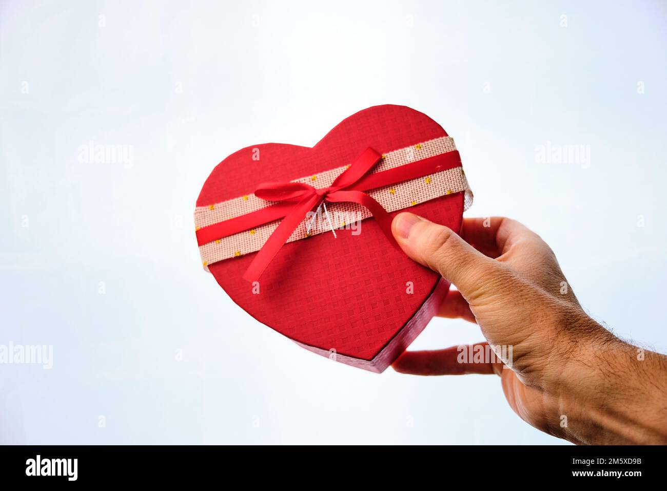 Man's hand giving a gift in the shape of a heart on a white background ...