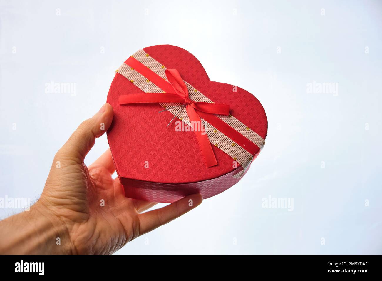Man's hand giving a gift in the shape of a heart with a bow, on a white ...