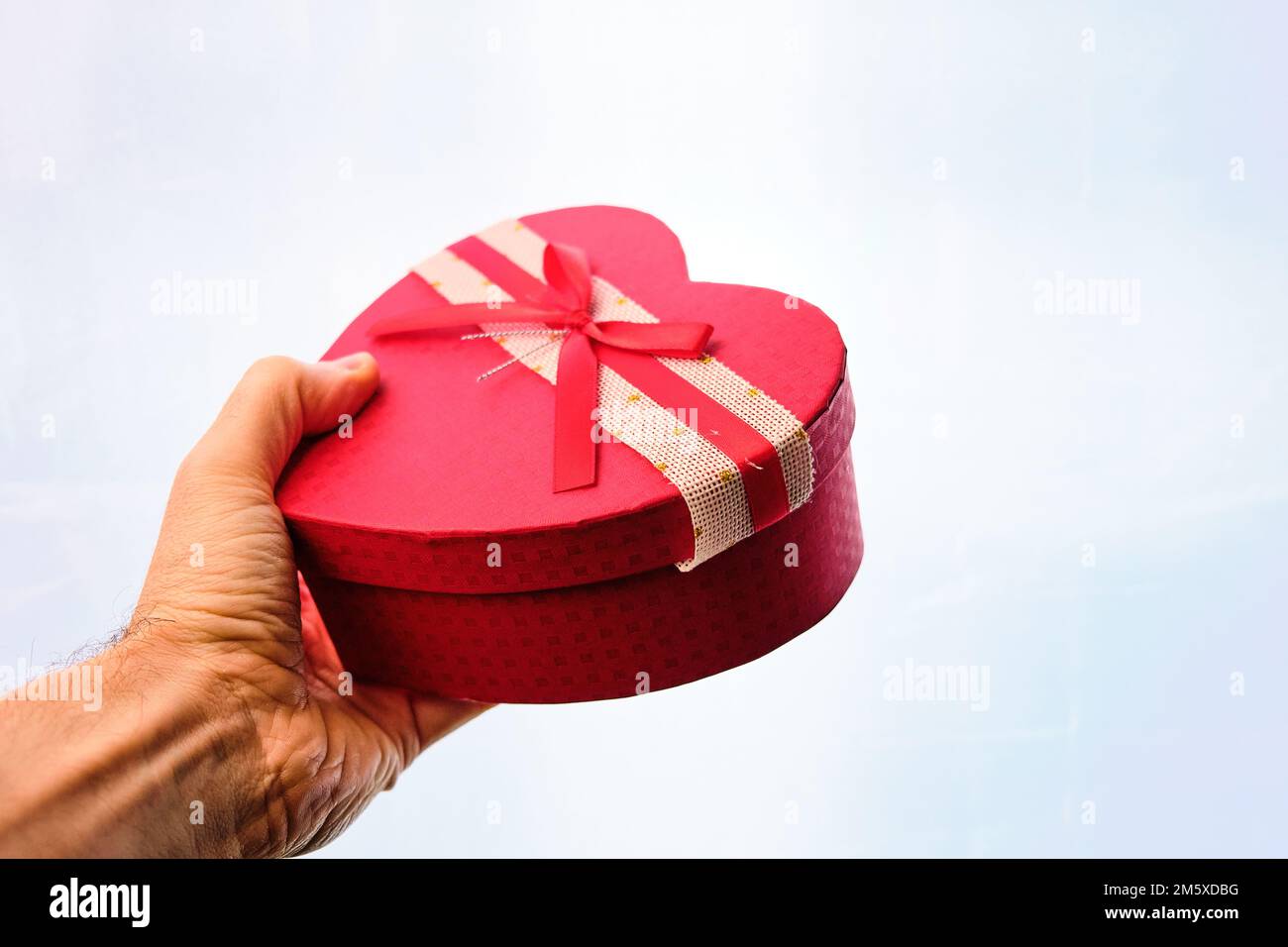 Man's hand giving a gift in a heart-shaped box with a bow, on a white ...