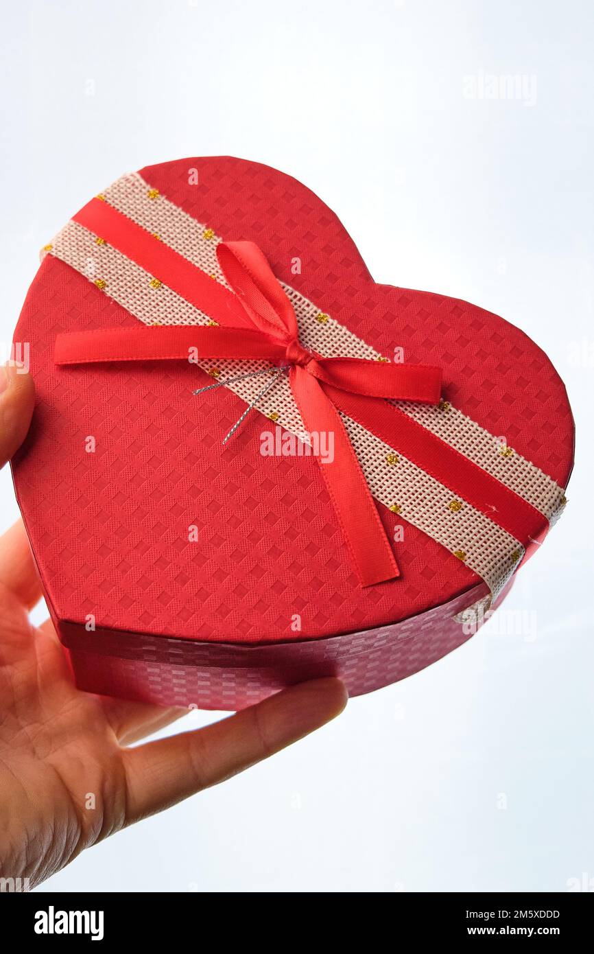 Man's hand giving a gift in the shape of a heart with a bow, on a white ...
