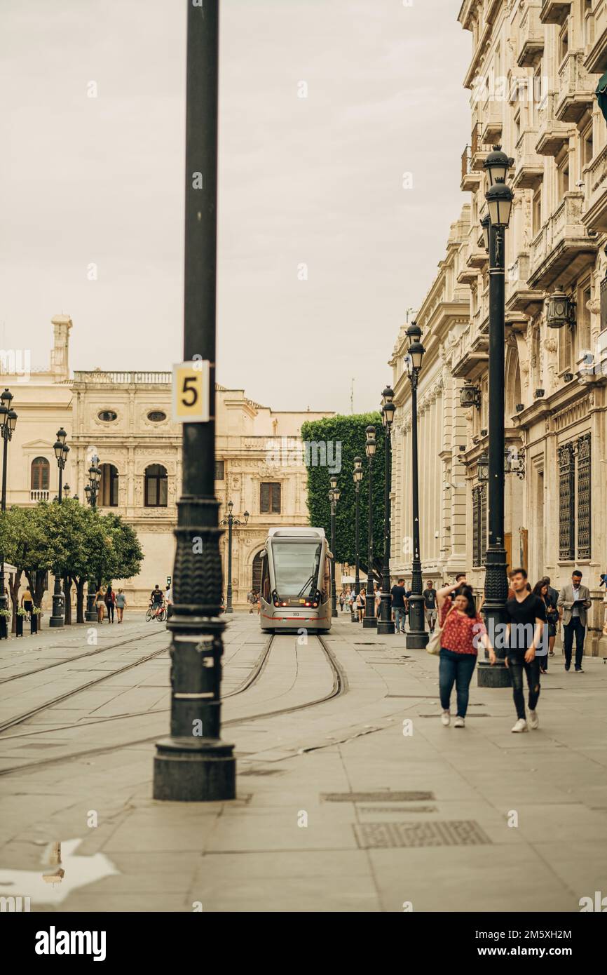 A vertical shot of people walking in a street next to a tram in Sevilla ...