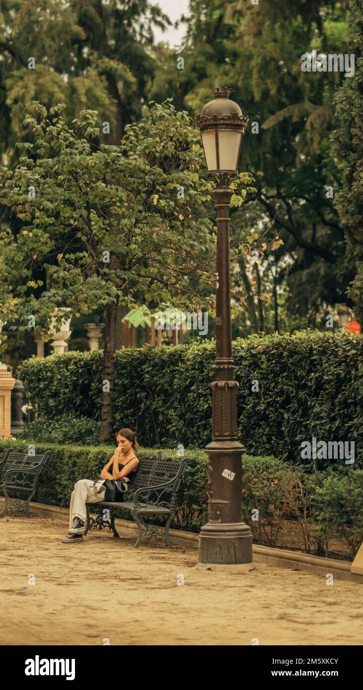 A vertical shot of a girl sitting on bench in a park in Seville, Spain ...