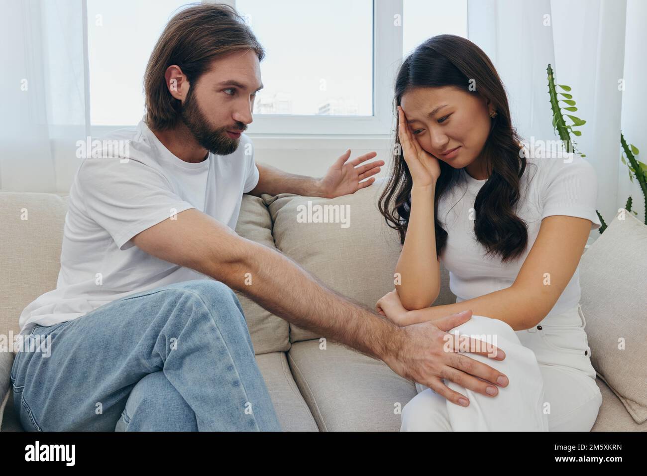A sad Asian woman talks to a man in tears at home sitting on the couch ...