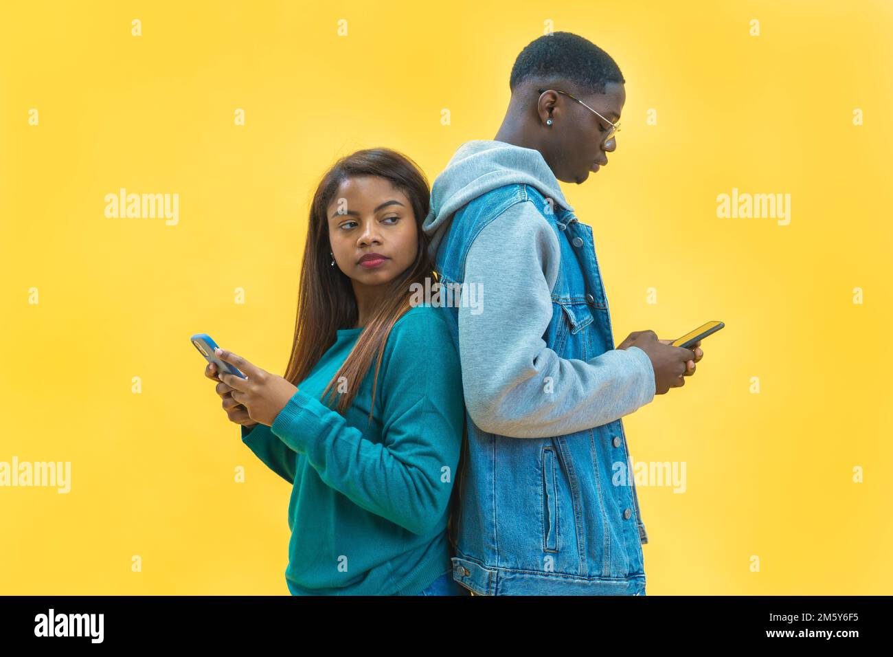 Black millennial couple using smartphones - Social network addiction - Isolated yellow ...