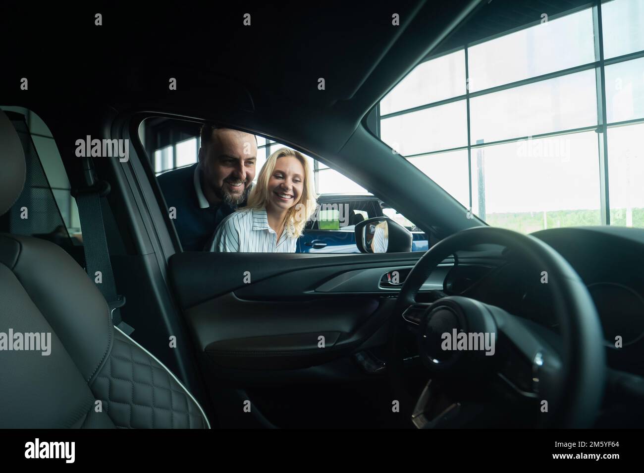 Caucasian family couple looking out the car window in a car dealership ...