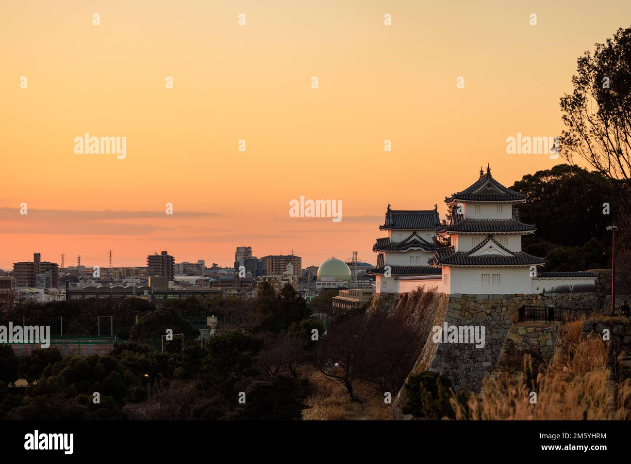 Japanese castle atop stone wall overlooking city skyline at sunset ...