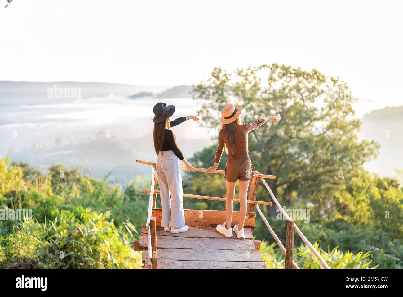 Sunrise morning 2 traveler girls stand on mountain view platform look ...