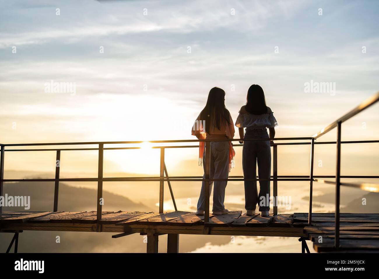 Sunrise morning 2 traveler girls stand on mountain view platform look ...