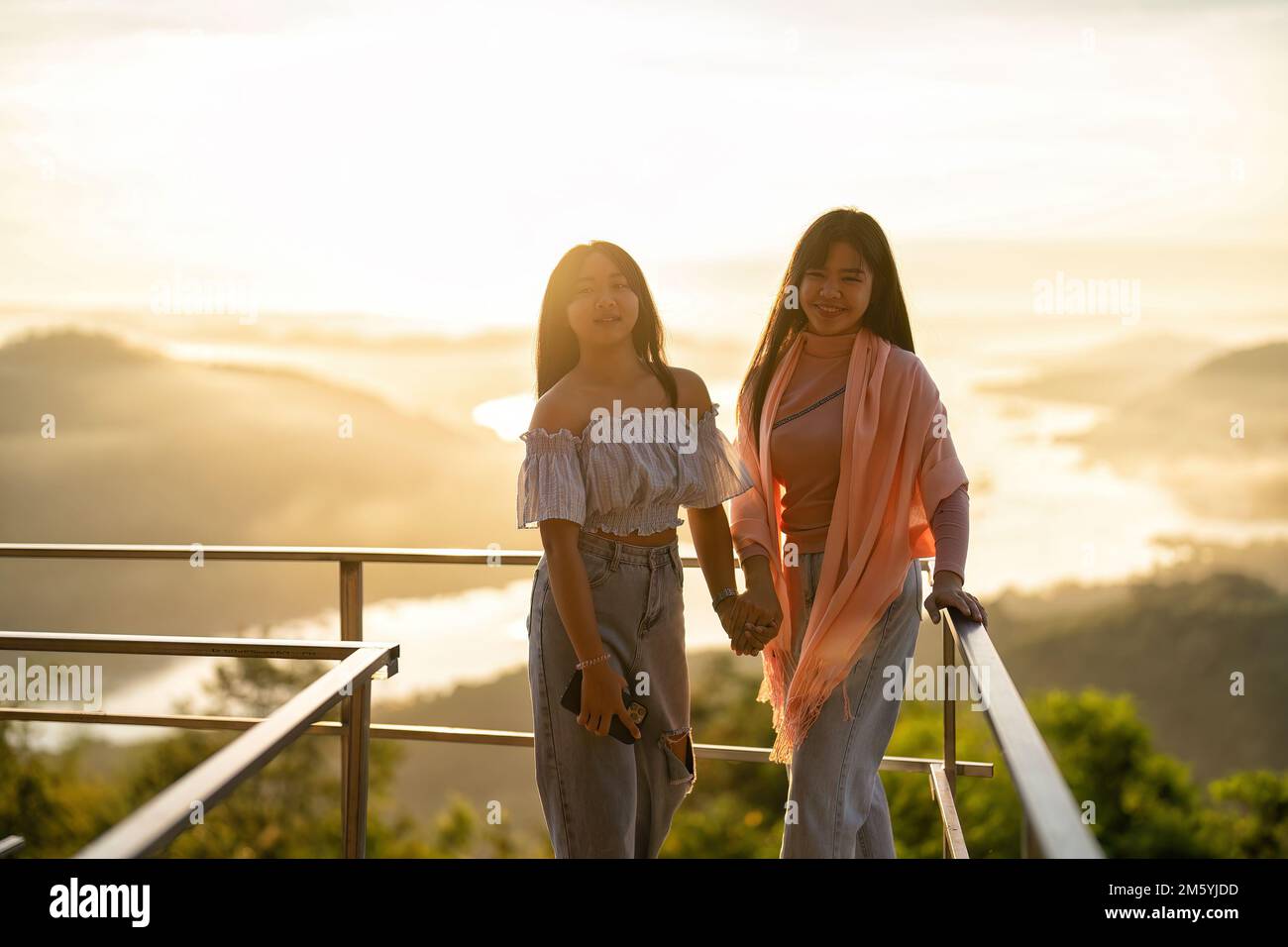 Sunrise morning 2 traveler girls stand on mountain view platform look ...