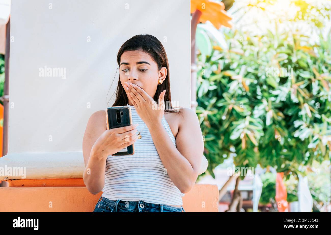 Girl with cell phone with a surprised face leaning on a wall. Young ...