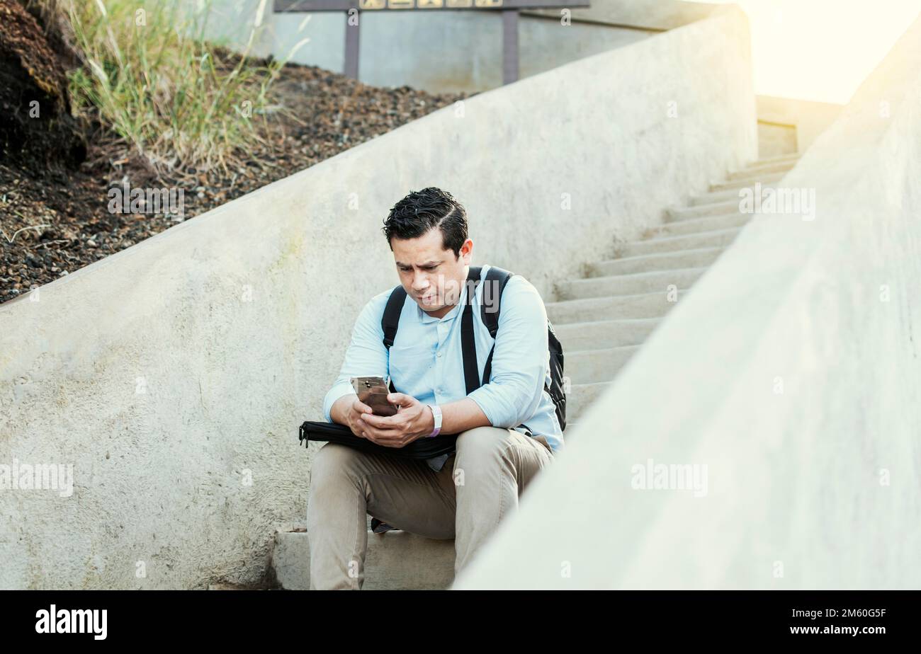 A guy sitting on stairs using his cell phone outdoors with copy space ...