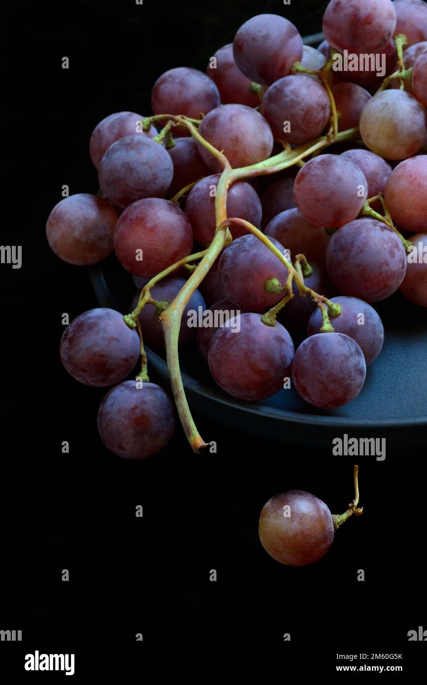 Red grape vine (Vitis vinifera) on plate against dark background Stock ...
