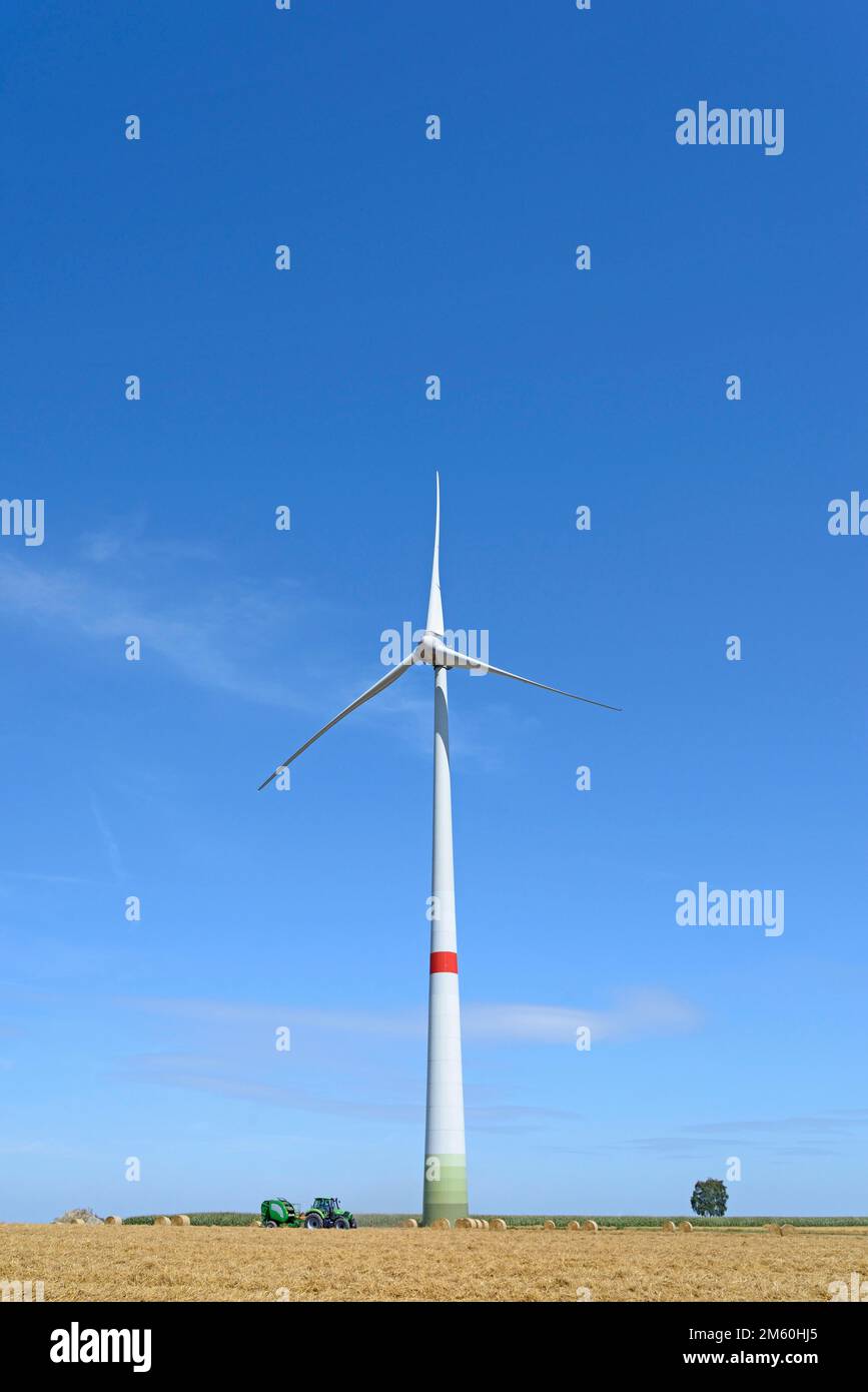 Wind turbine at a stubble field with round bales of straw, blue sky ...