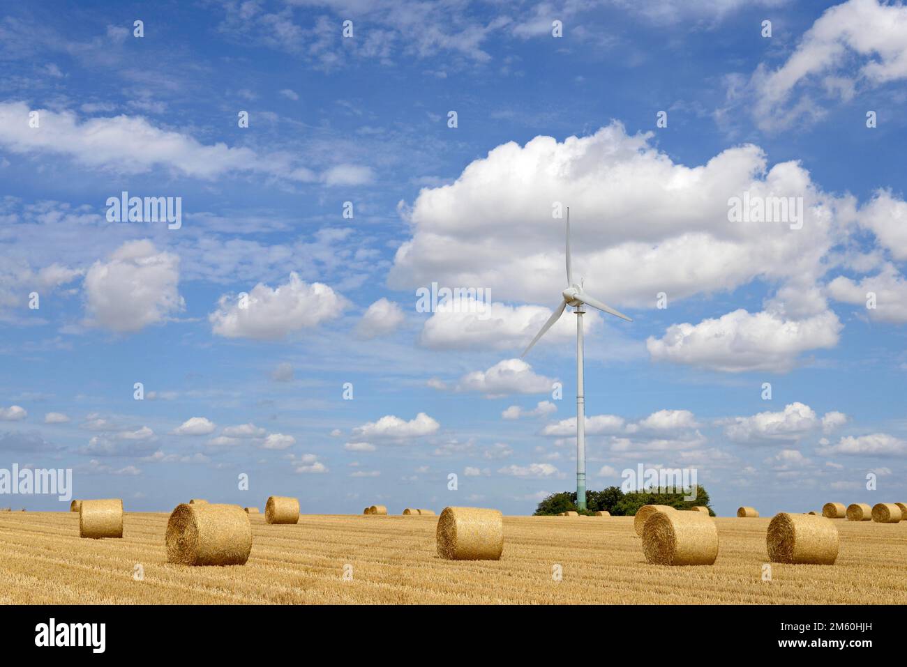 Wind turbine at a stubble field with round bales of straw, blue cloudy ...