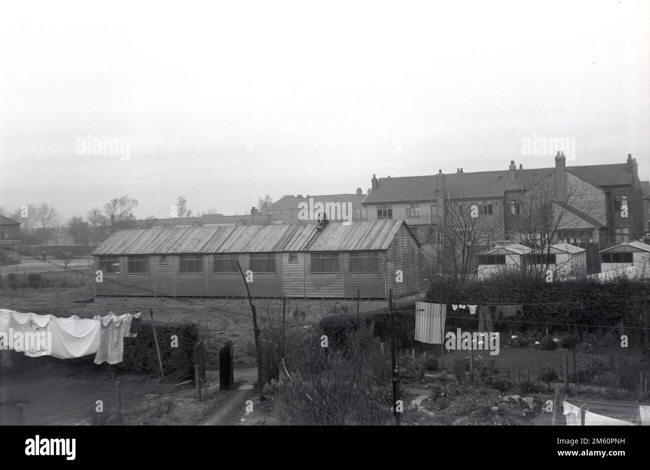 1950s, historical, on a long wooden hut, a man on its roof, mending ...
