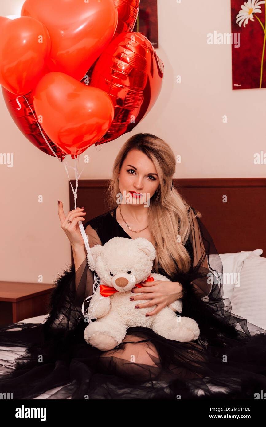 A beautiful woman in a black peignoir on a bed with red balloons. Women ...