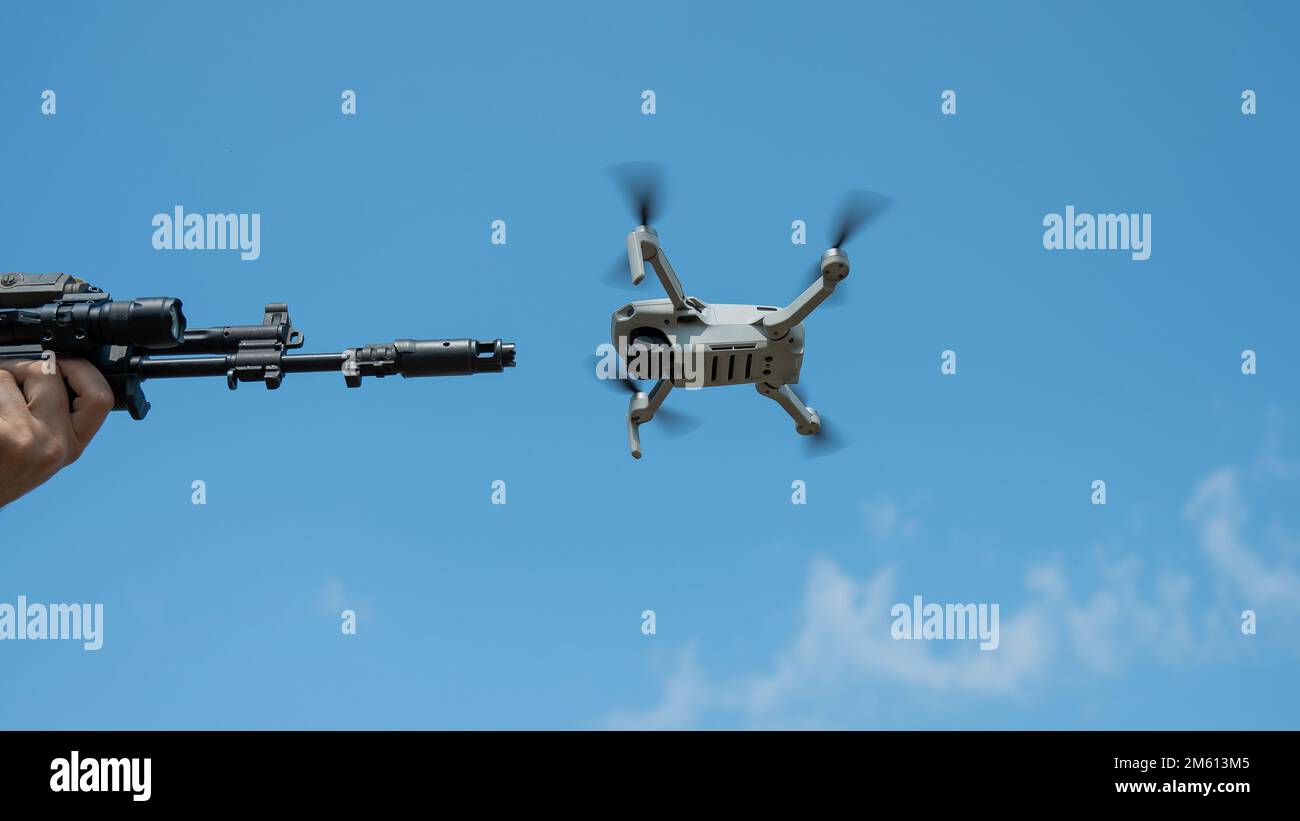A man aims to shoot a rifle at a flying drone against a blue sky Stock ...
