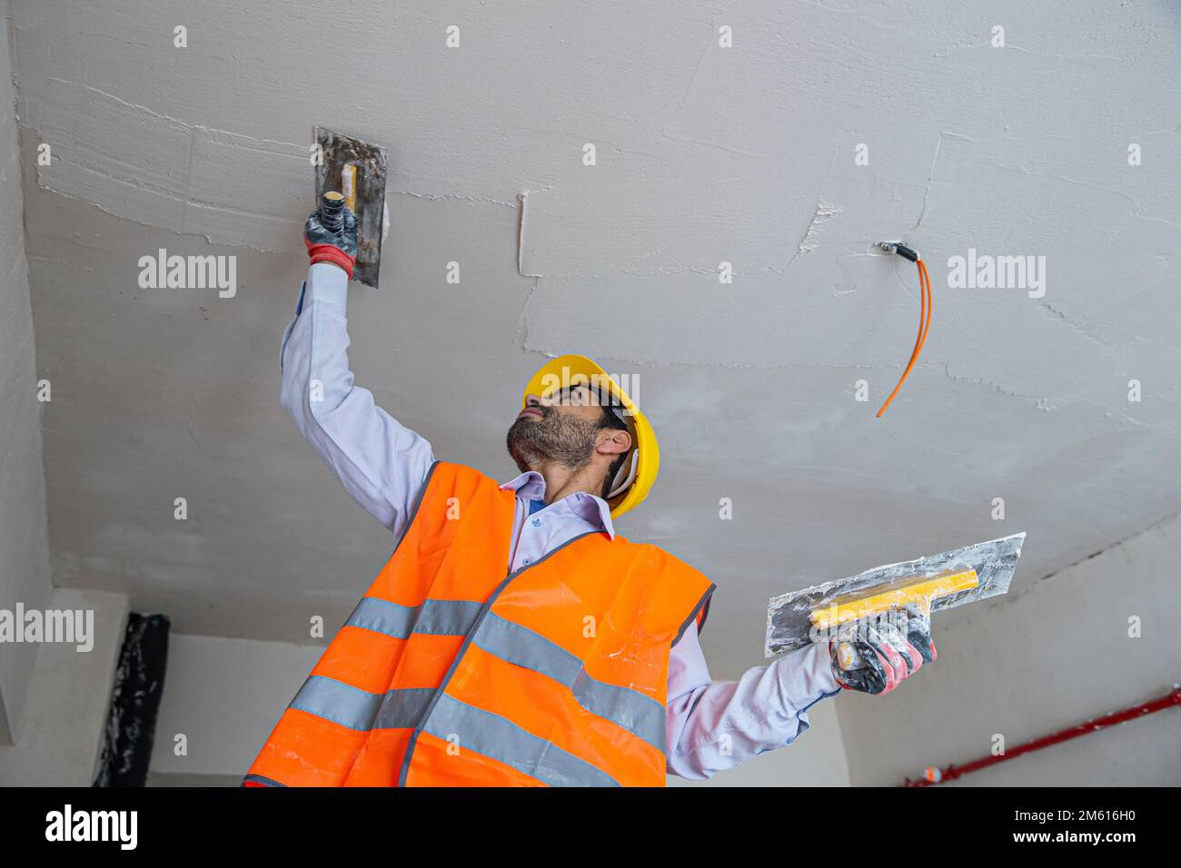A plasterer in construction wears overalls and a hat. He is plastering ...