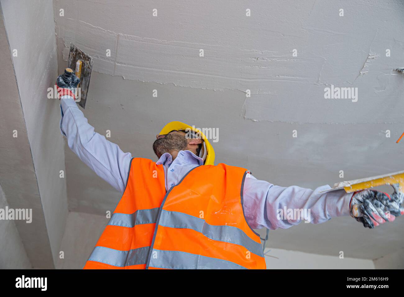 A plasterer in construction wears overalls and a hat. He is plastering ...