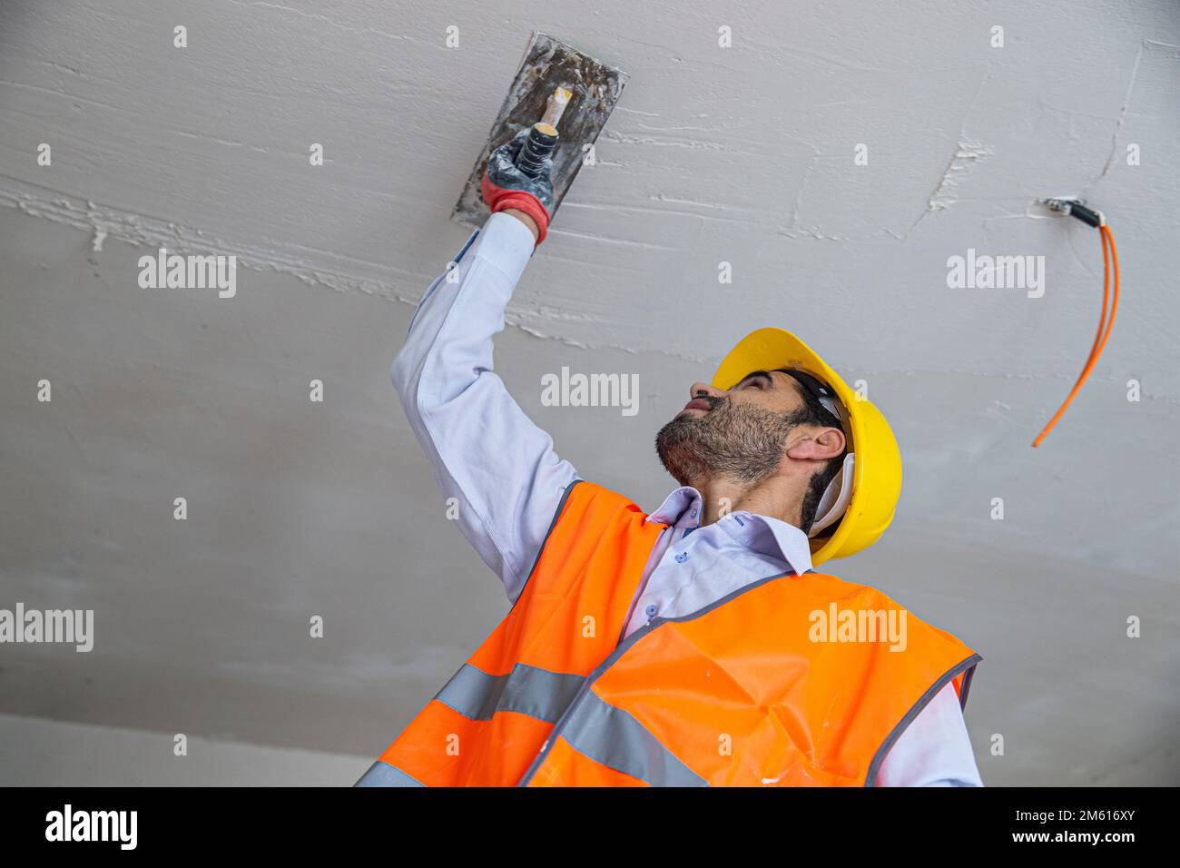 A plasterer in construction wears overalls and a hat. He is plastering ...