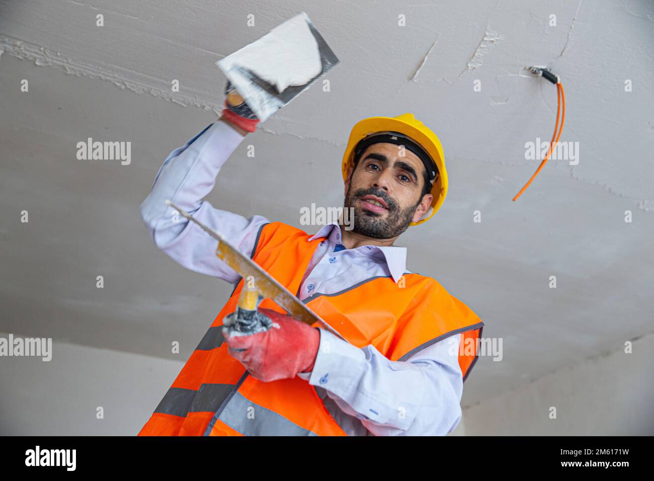 A plasterer in construction wears overalls and a hat. He is plastering ...
