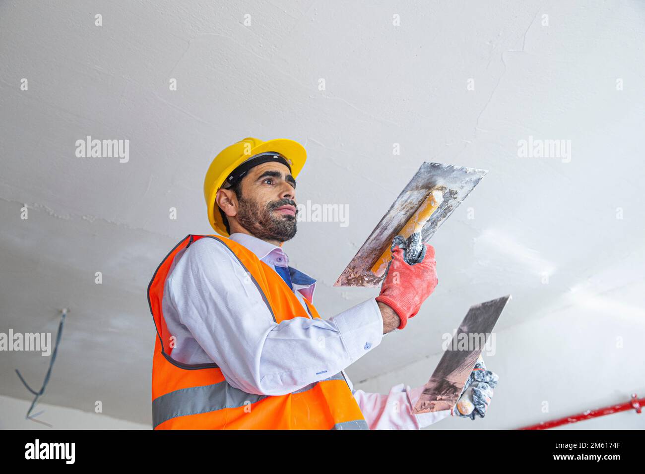 A plasterer in construction wears overalls and a hat. He is plastering ...