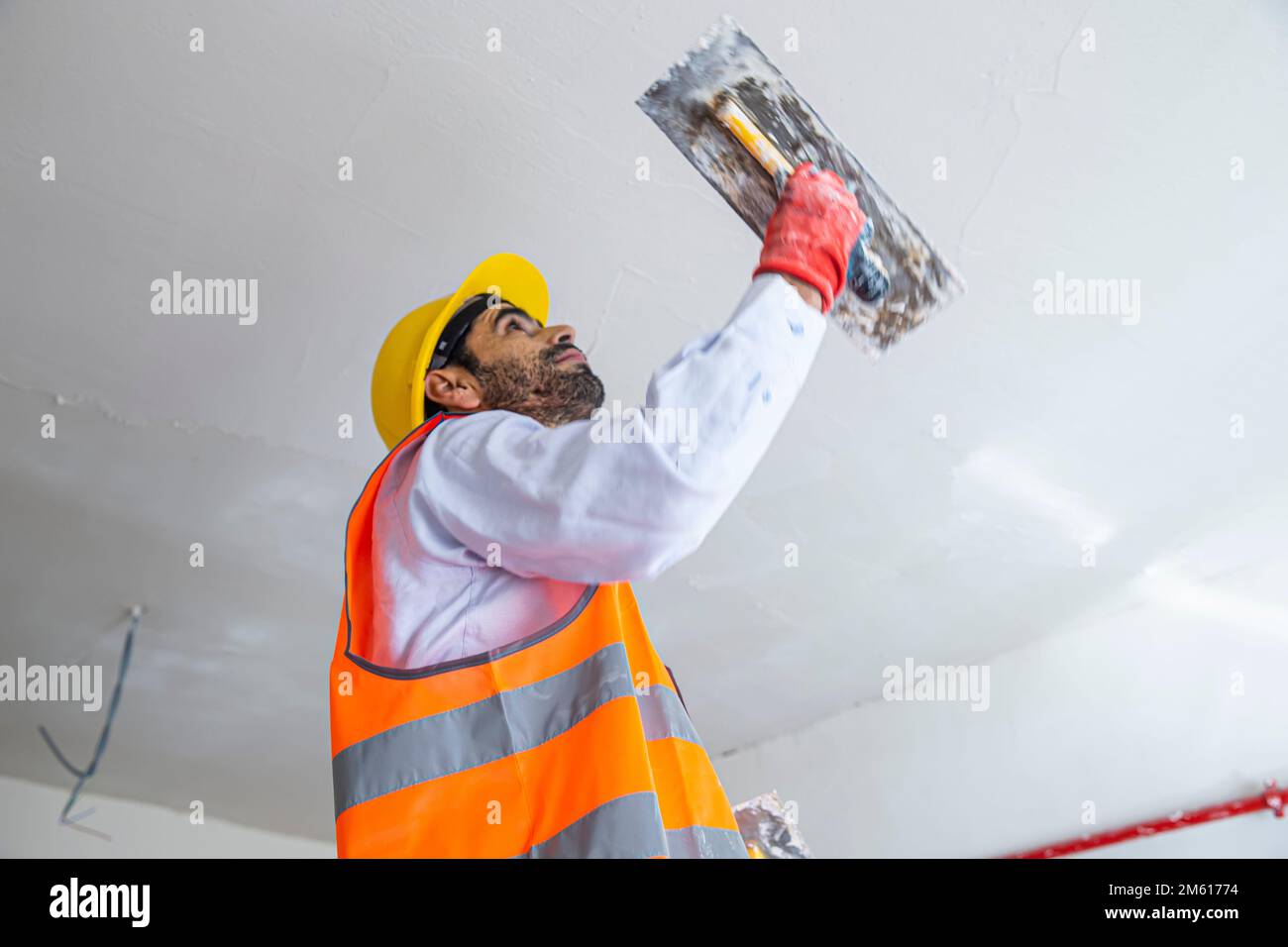 A plasterer in construction wears overalls and a hat. He is plastering ...