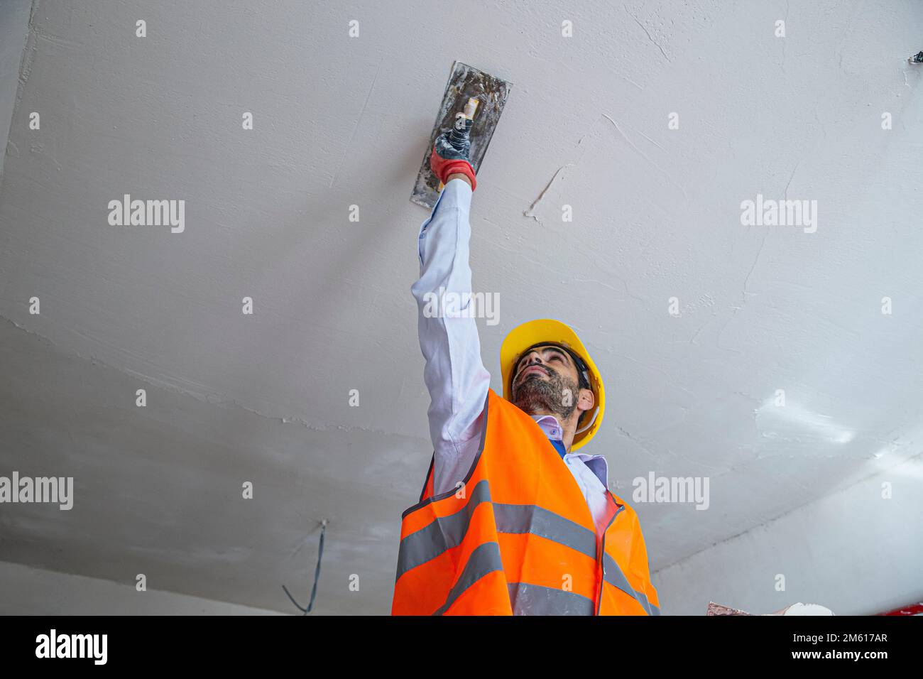 A plasterer in construction wears overalls and a hat. He is plastering ...